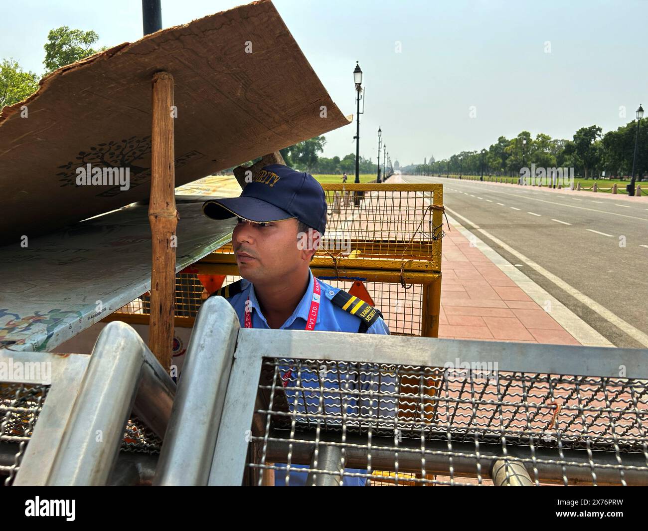 A private security guard stands under the shade of a used plyboard ...