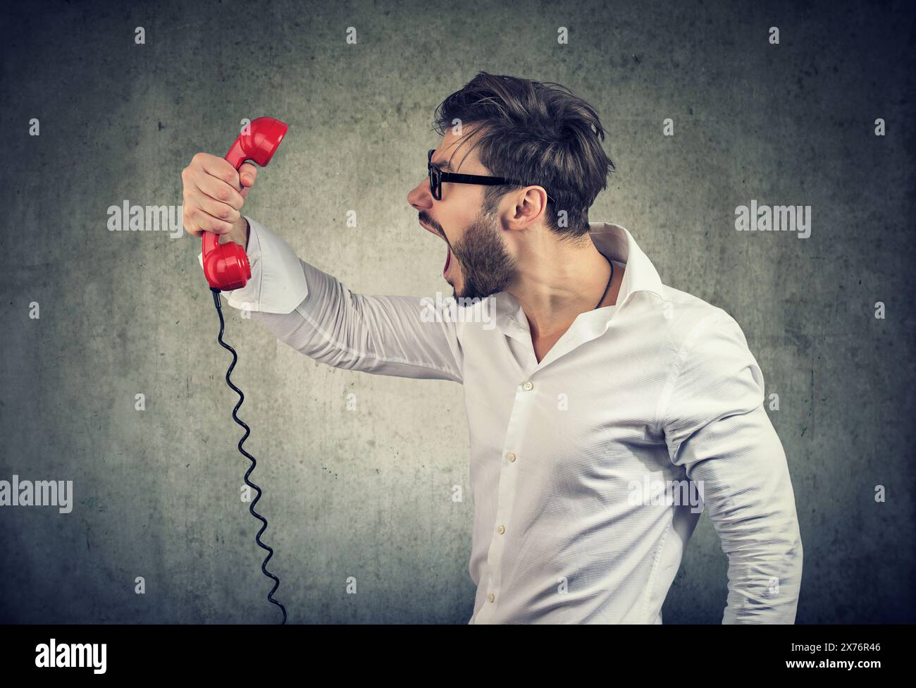 Side view of casual bearded young man holding red telephone receiver ...