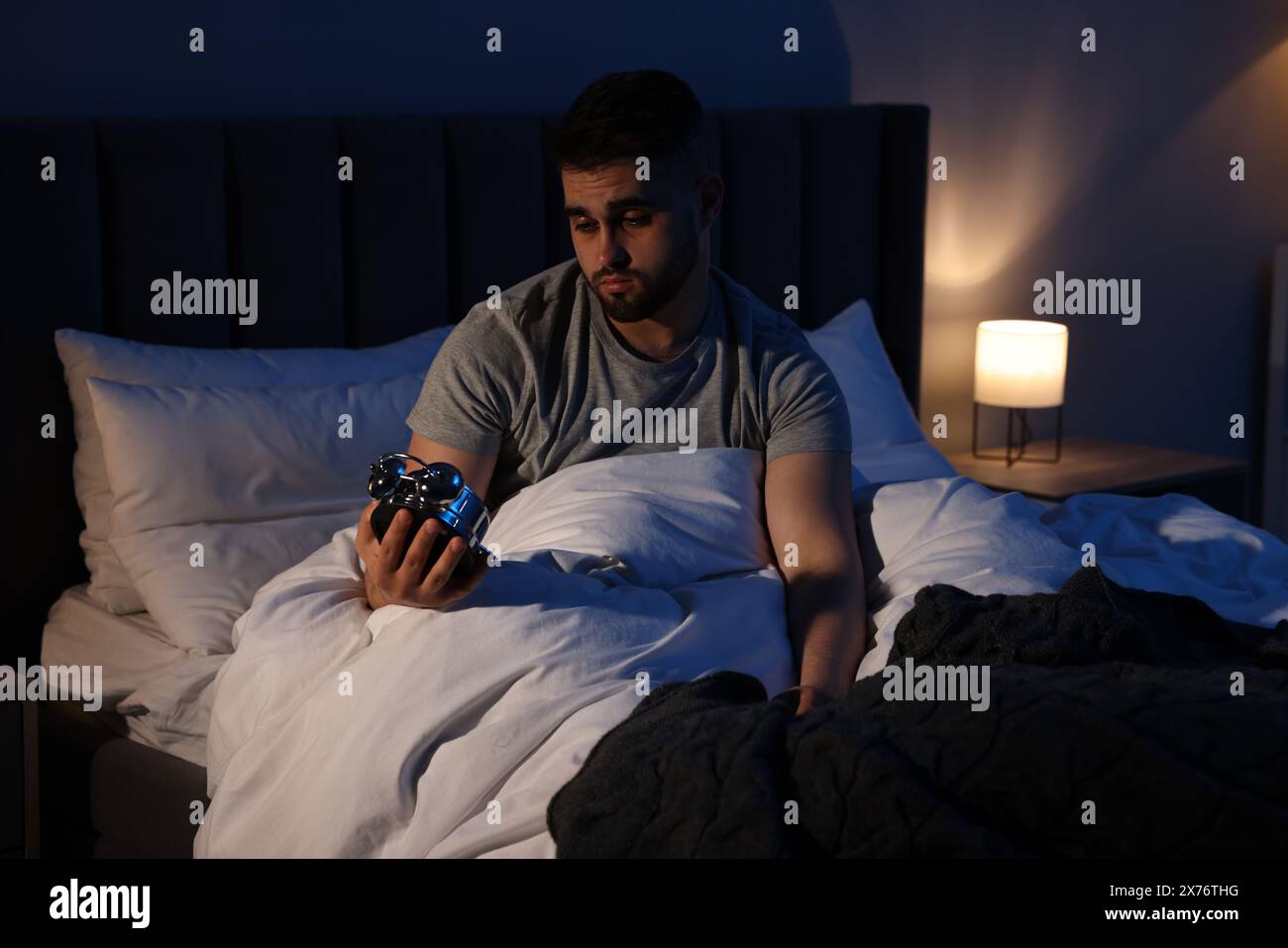 Sleepy man looking at alarm clock in bed Stock Photo - Alamy