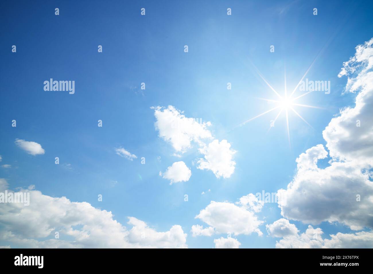 The sun peers through the cumulus clouds in the cerulean sky, creating ...
