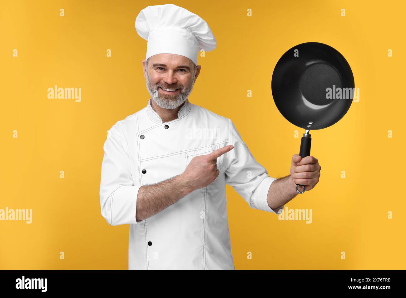 Happy chef in uniform pointing at wok on orange background Stock Photo ...