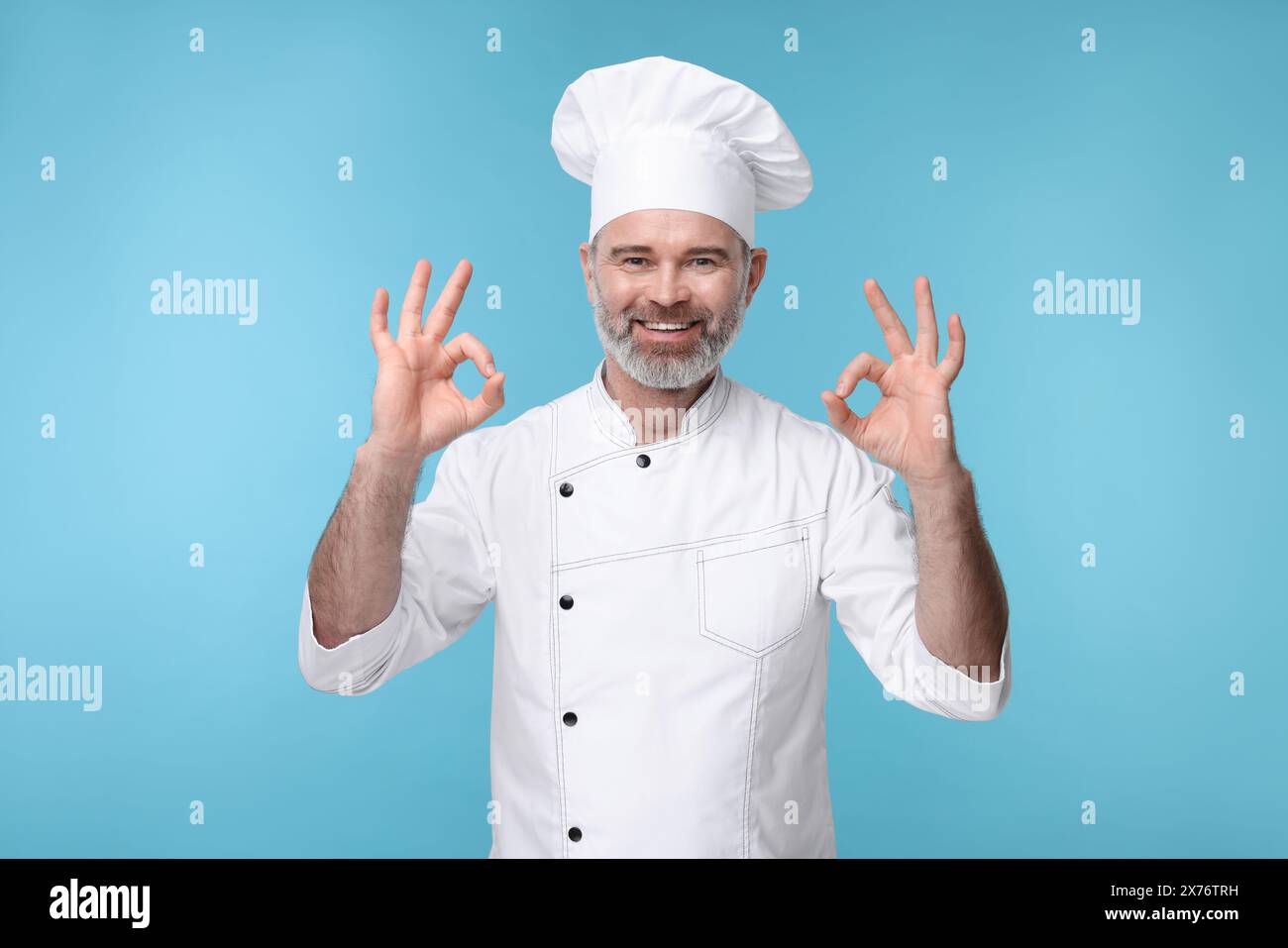 Happy chef in uniform showing OK gesture on light blue background Stock ...