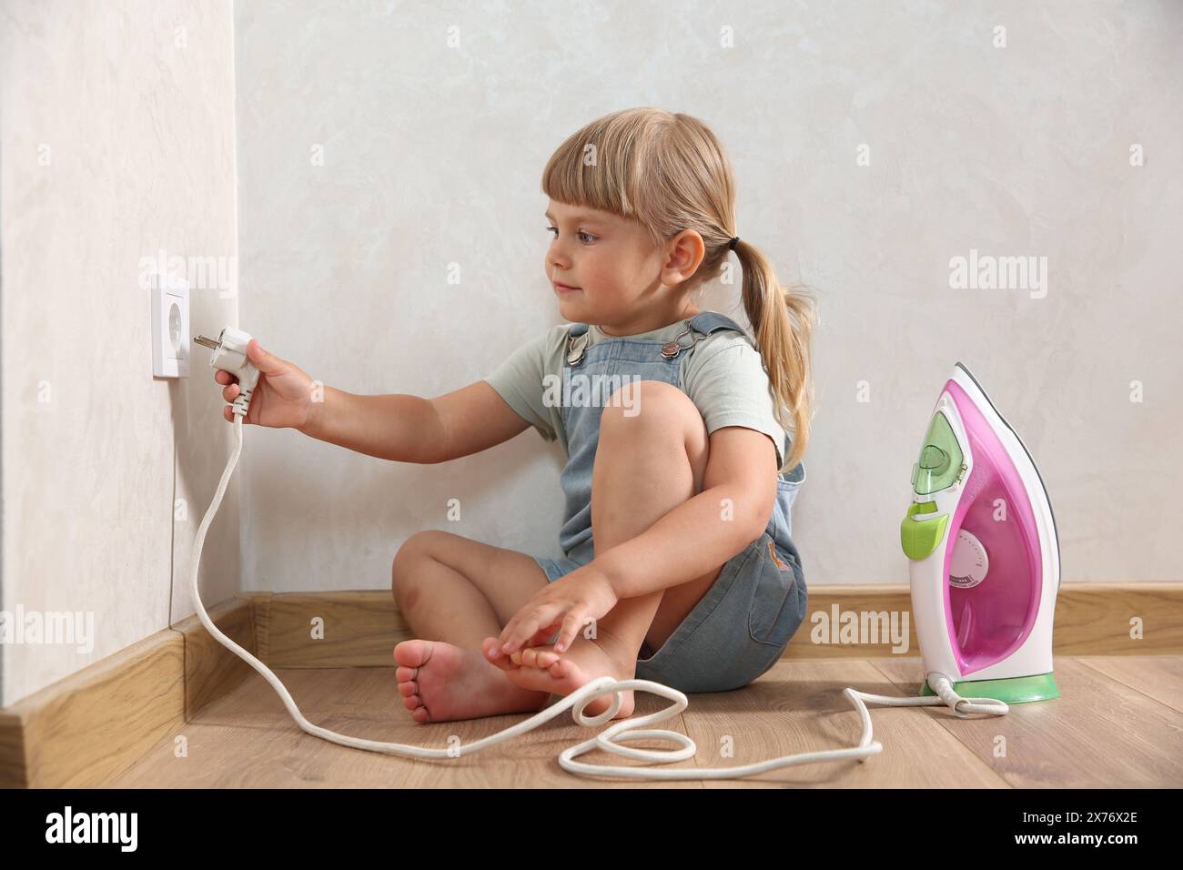 Little child playing with electrical socket and iron plug at home ...