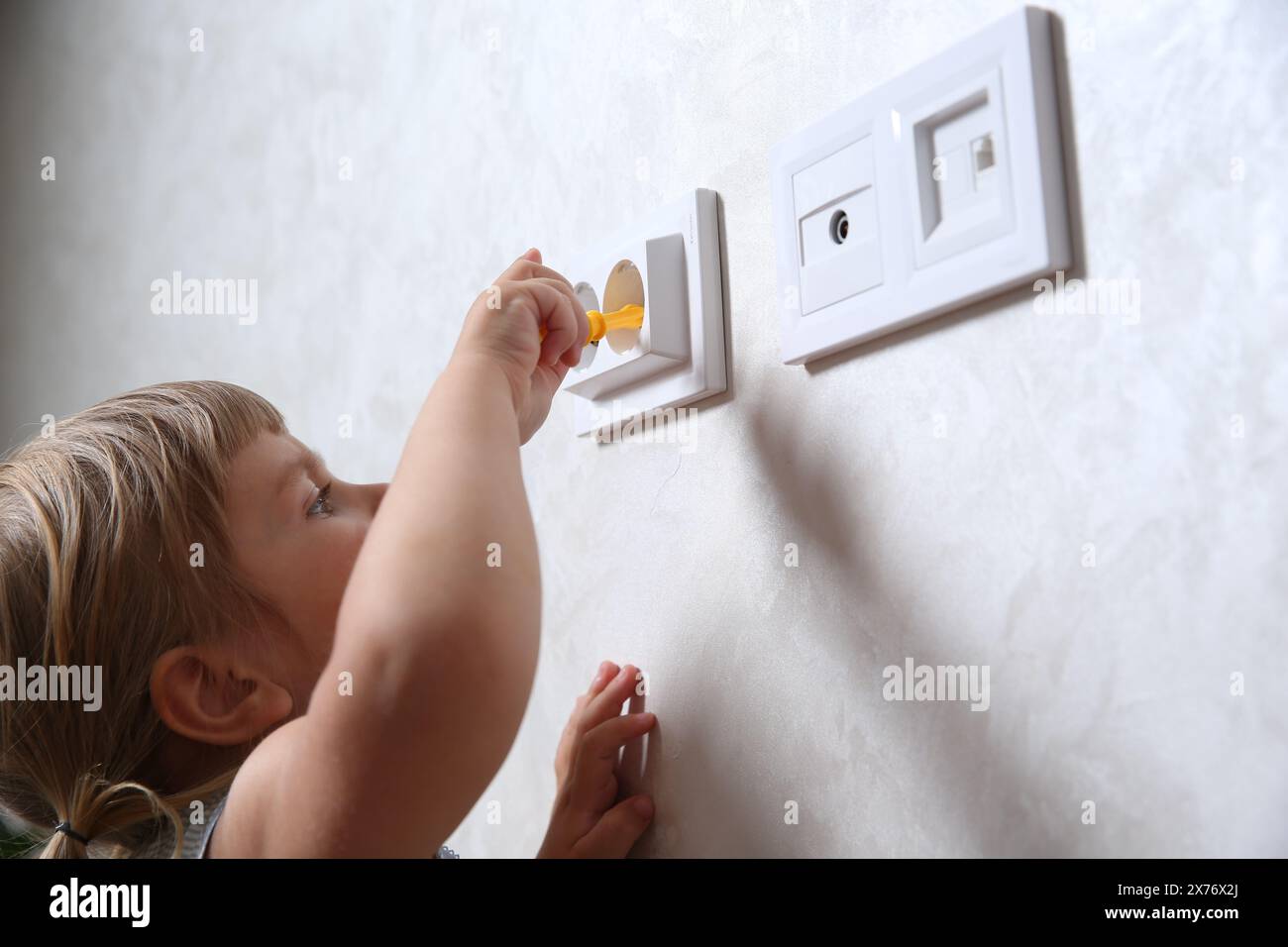 Little child playing with toy screwdriver and electrical socket at home ...