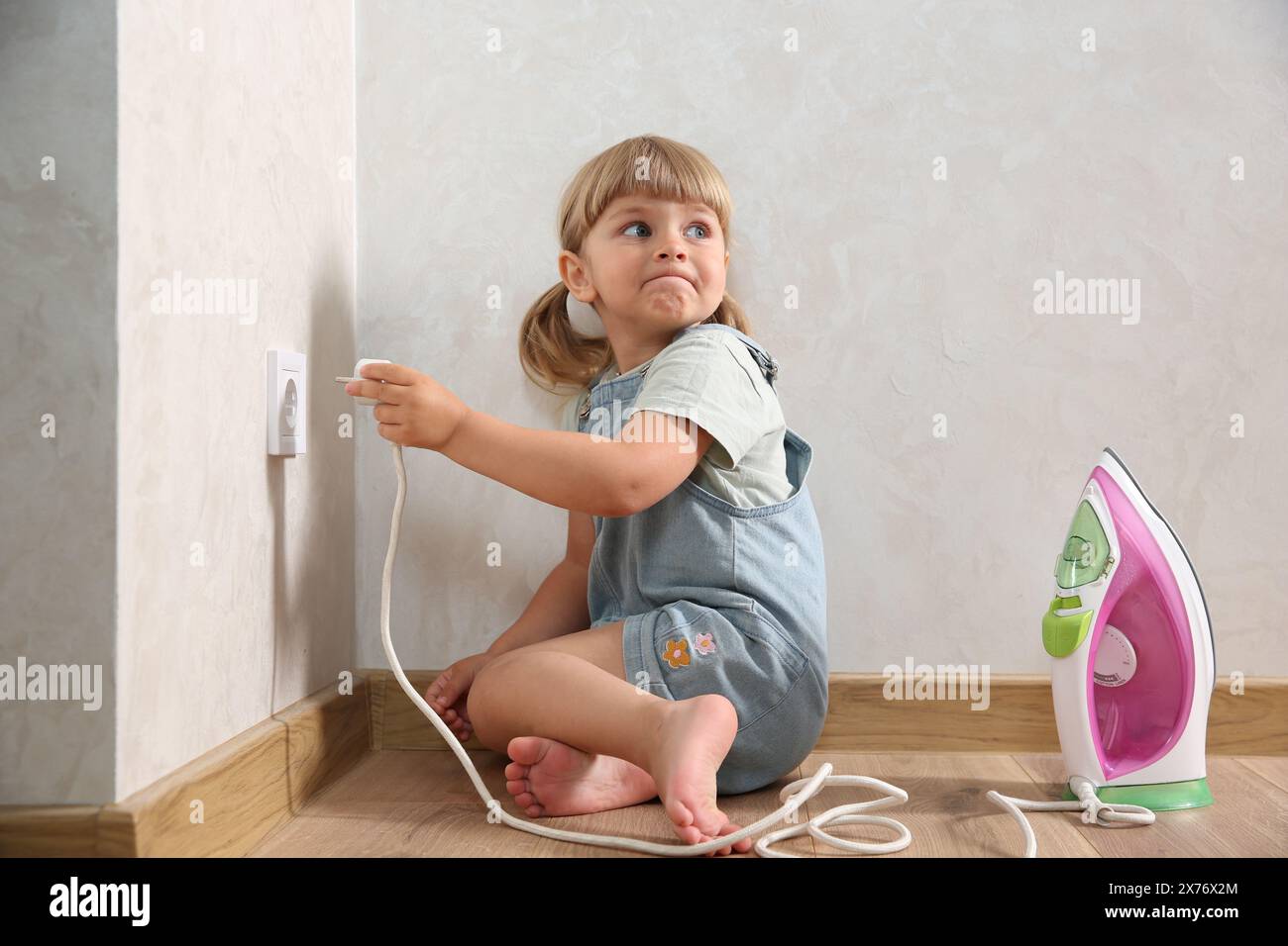 Little child playing with electrical socket and iron plug at home ...