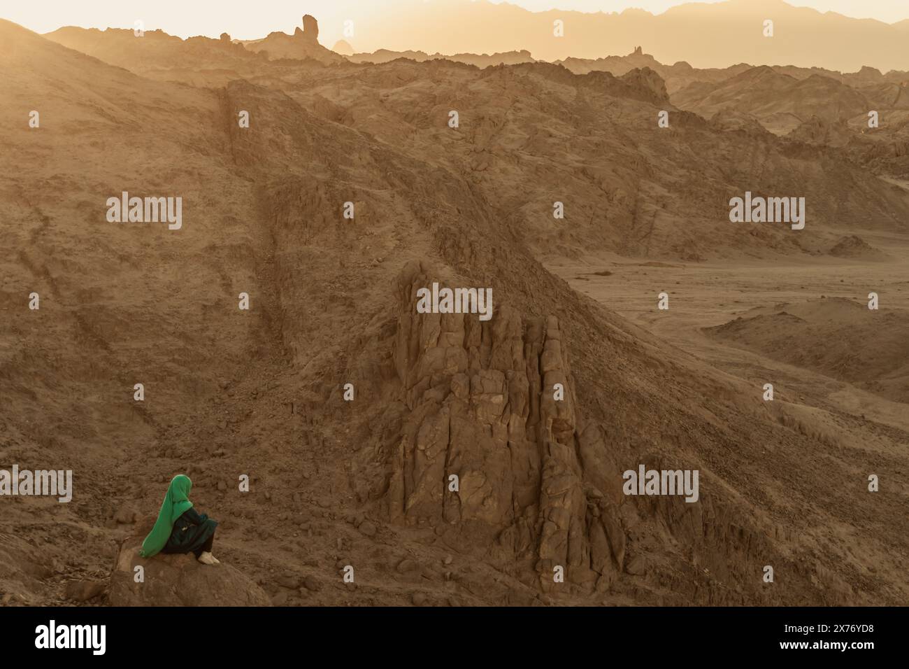 Veiled young girl sits alone in rugged rocky landscape at dusk Stock ...