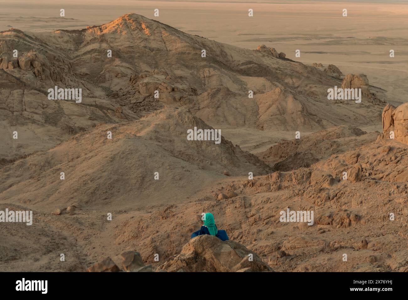 Veiled young girl sits alone in rugged rocky landscape Stock Photo - Alamy