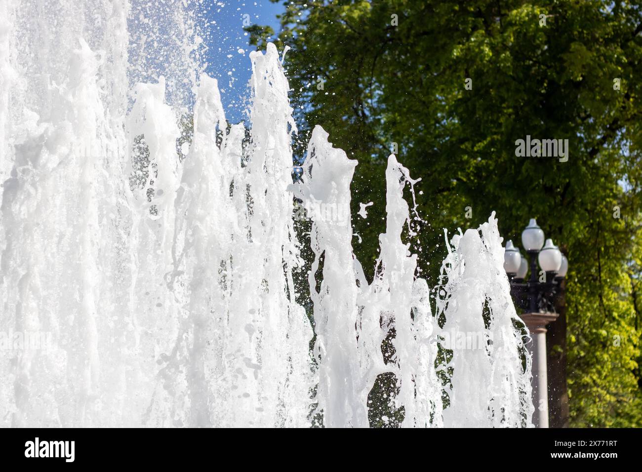 A fountain in a park with trees in the background, the flowing water ...