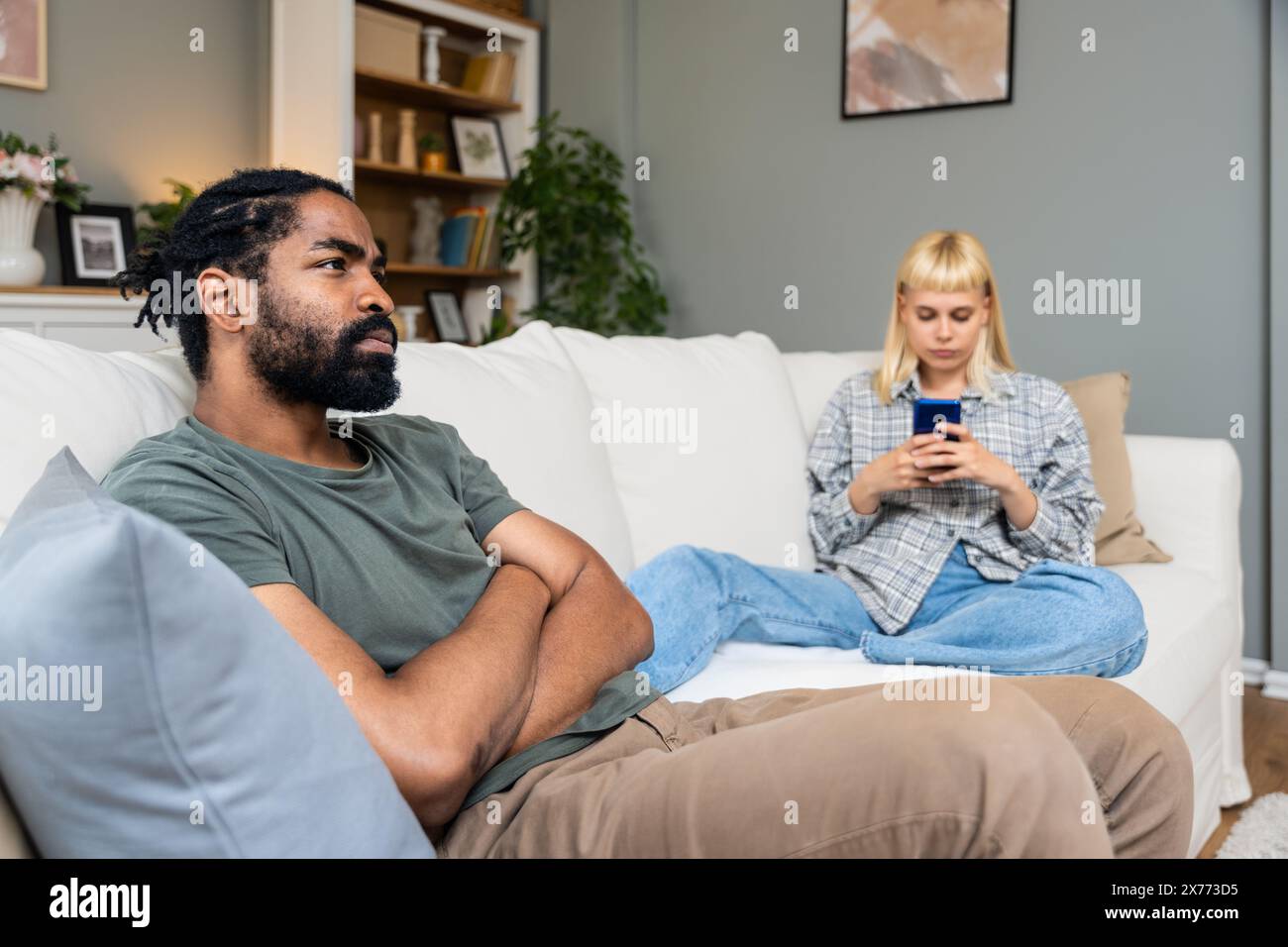Young couple sitting on sofa at home, woman ignoring man, typing text ...