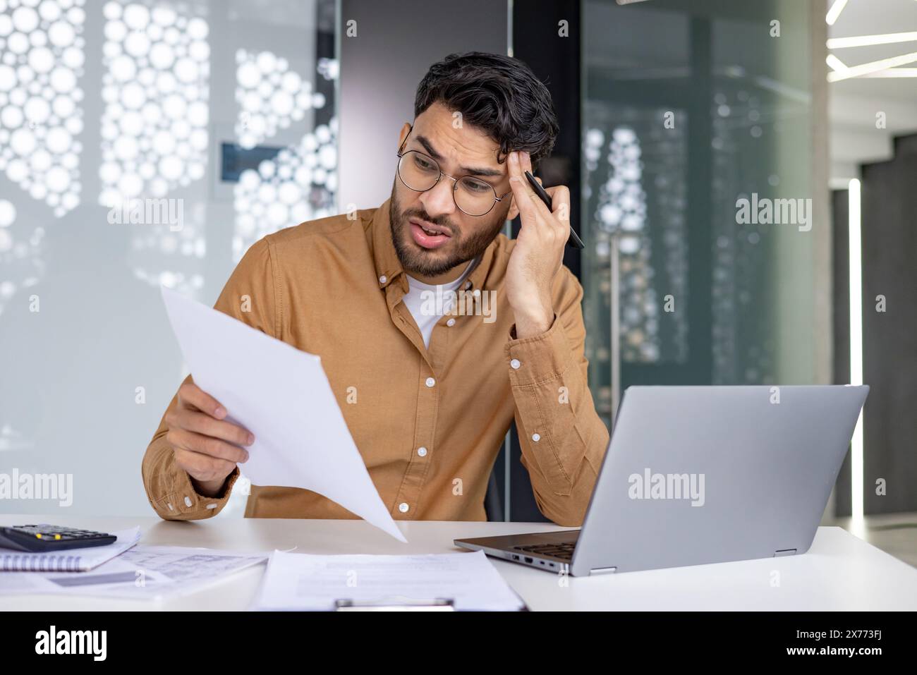 Stressed businessman analyzing documents at his desk in a modern office ...