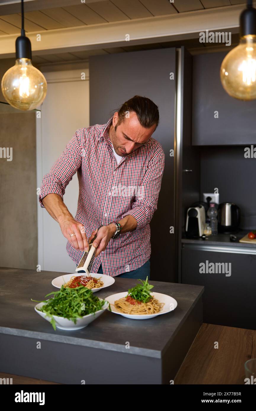 Vertical shot of young adult man grating cheese, seasoning the plate ...