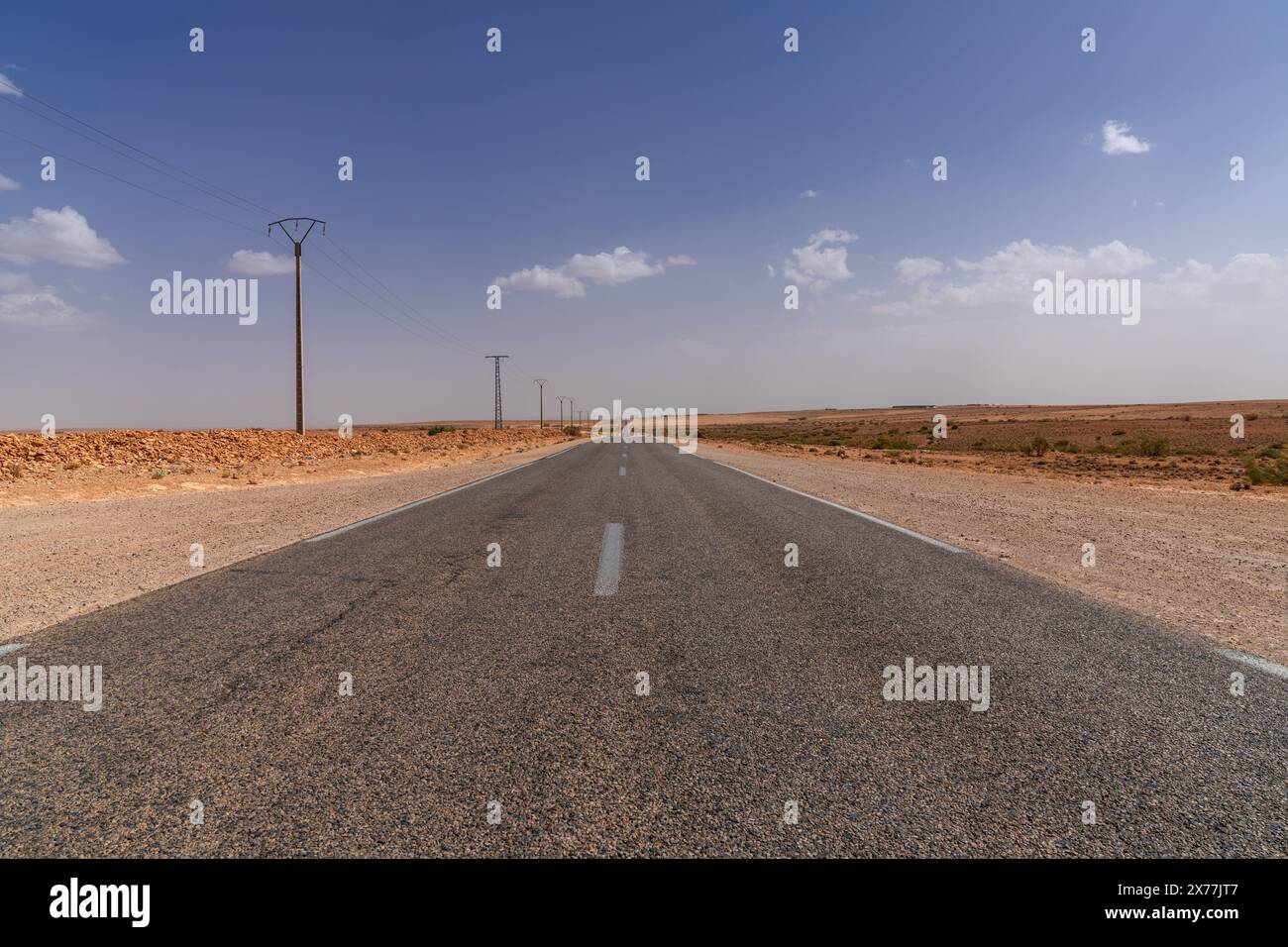 An endless desert highway and power lines leading through the rock and ...