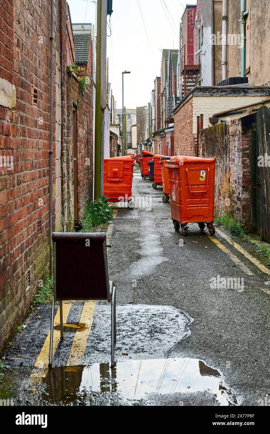 Row of orange coloured skips and unwanted chair in back alleyway Stock ...
