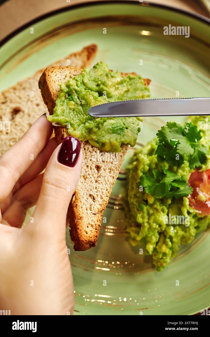 Female hands spreading guacamole on slice of toasted bread Stock Photo ...
