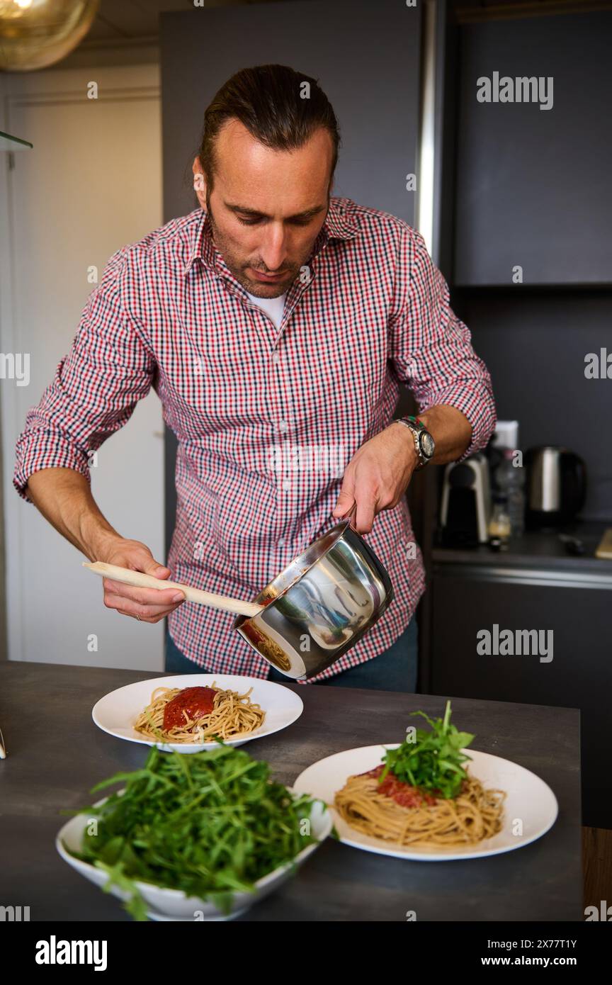 Attractive handsome European man pouring tomato sauce on spaghetti ...