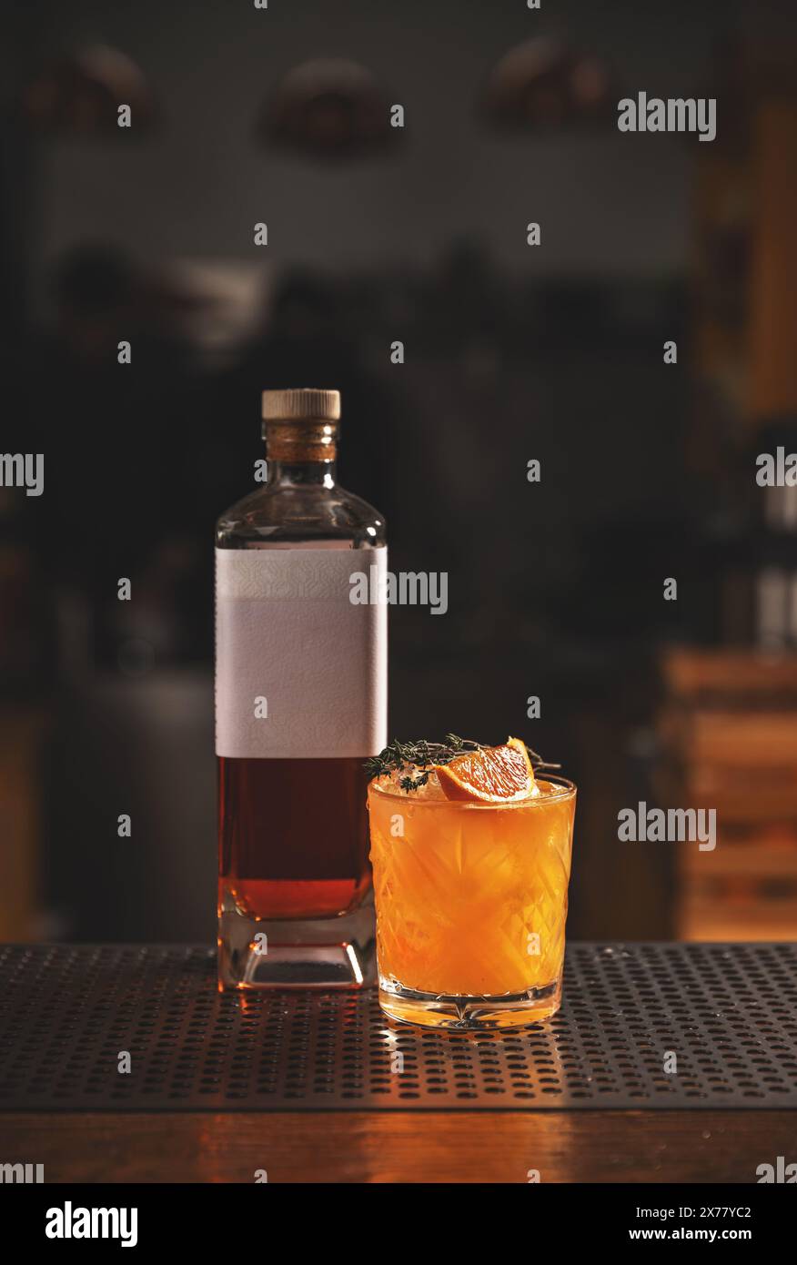 Elegant whiskey cocktail with orange garnish and bottle in a moody bar ...