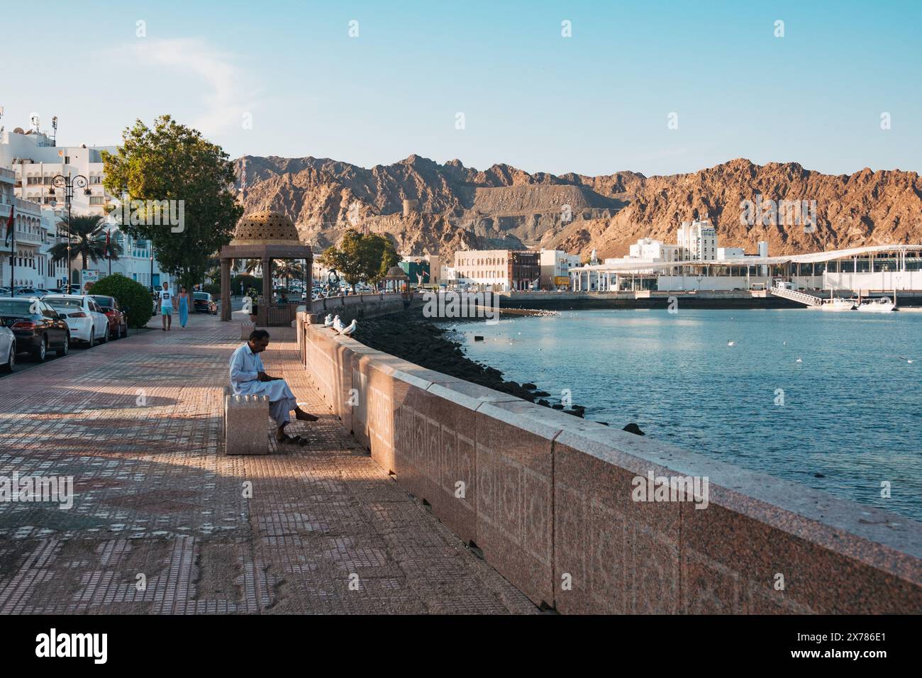 A man sits on a bench on the corniche at Sultan Qaboos Port, Muscat ...