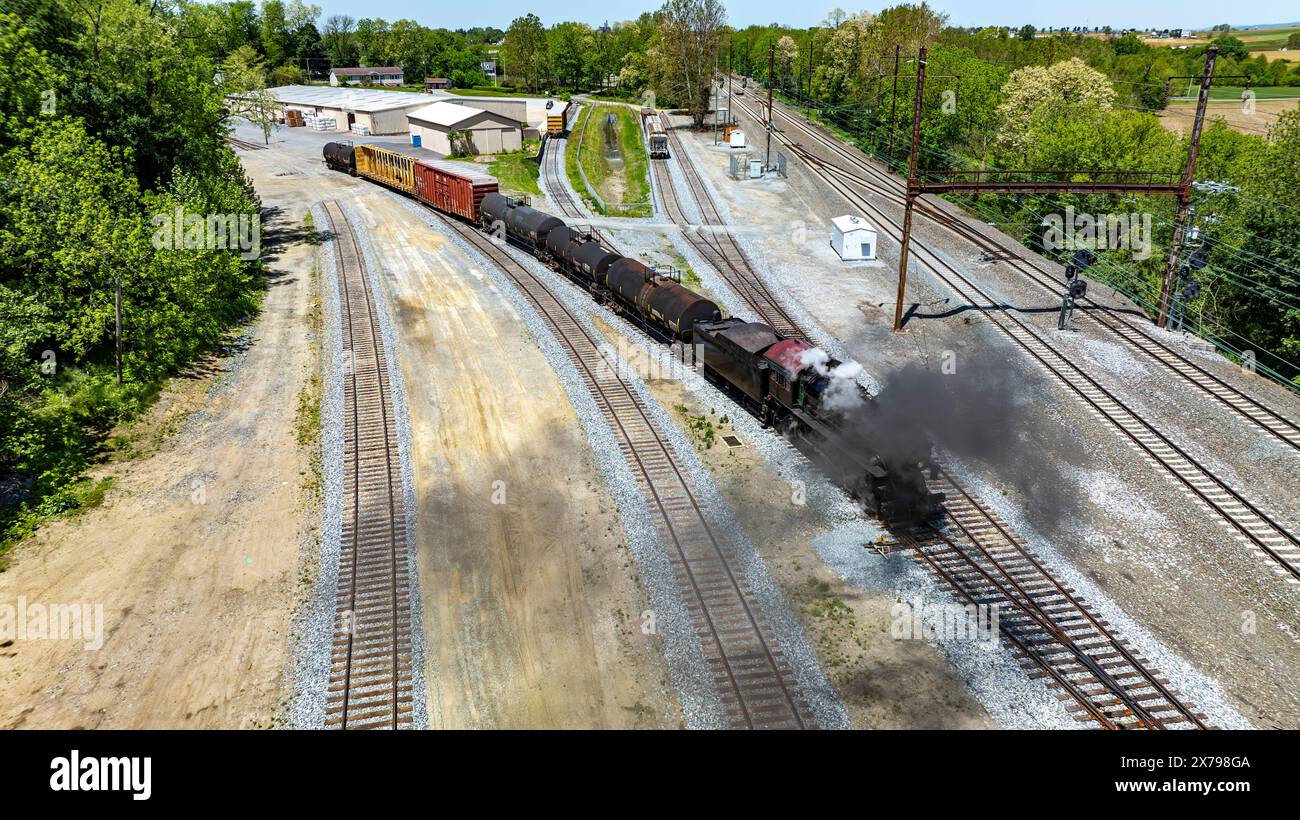 An aerial powerful vintage steam train moves through an industrial rail ...