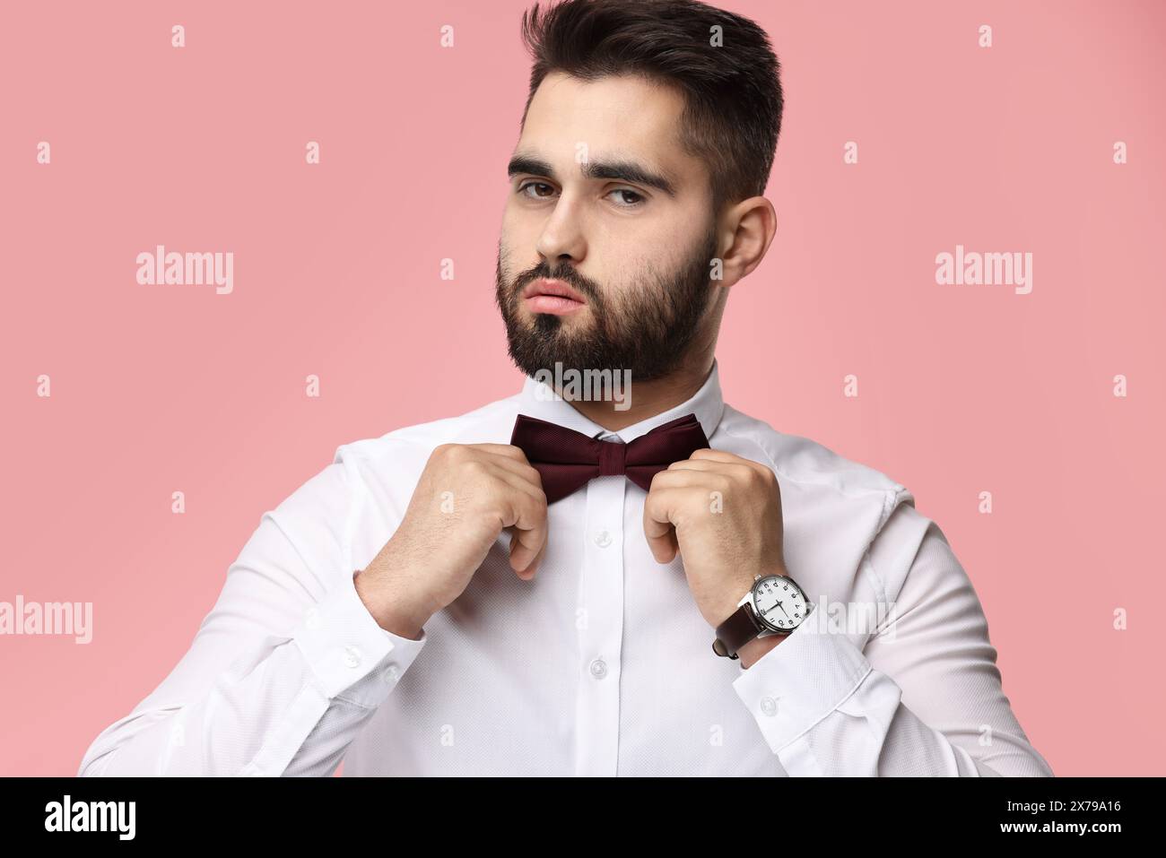 Portrait of handsome man adjusting bow tie on pink background Stock ...