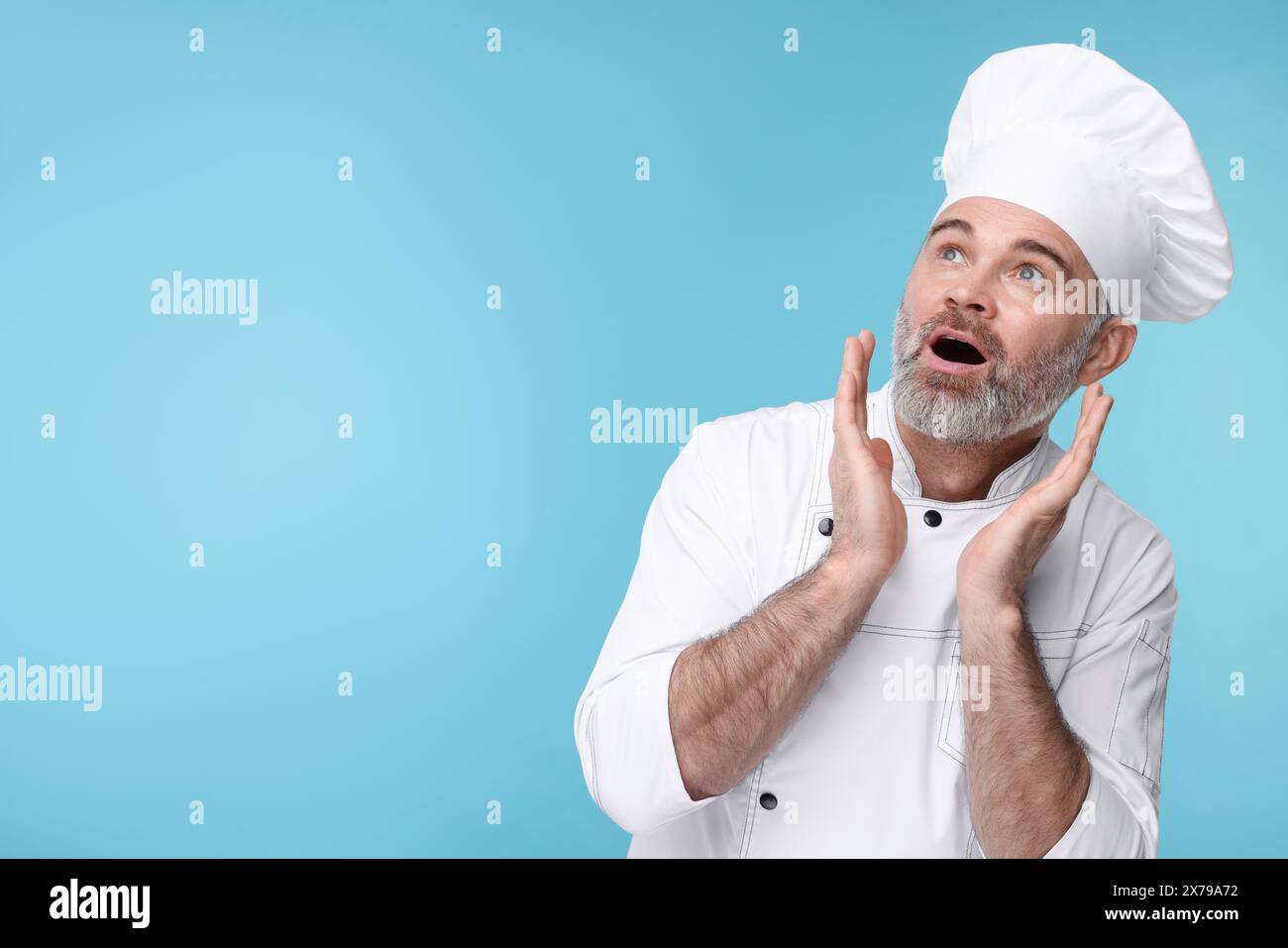 Surprised chef in uniform on light blue background, space for text ...