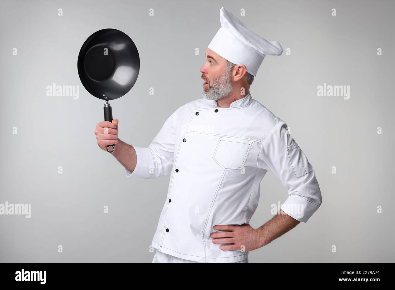 Surprised chef in uniform holding wok on grey background Stock Photo ...