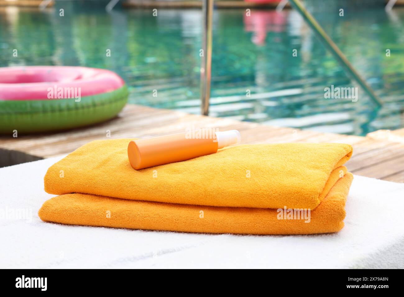 Beach towels and sunscreen on sun lounger near outdoor swimming pool ...