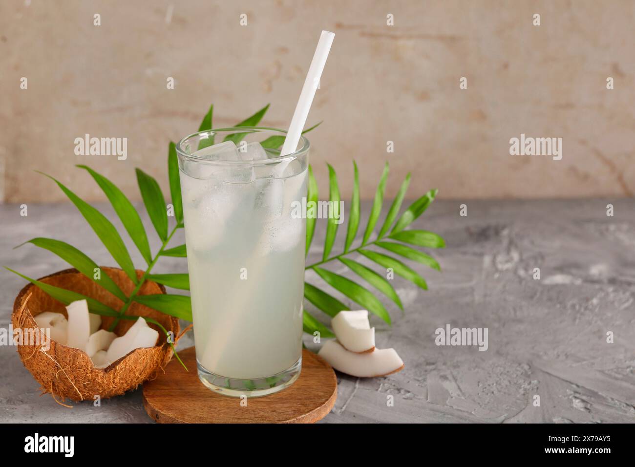 Glass of coconut water, ice cubes, leaves and nuts on grey table, space ...