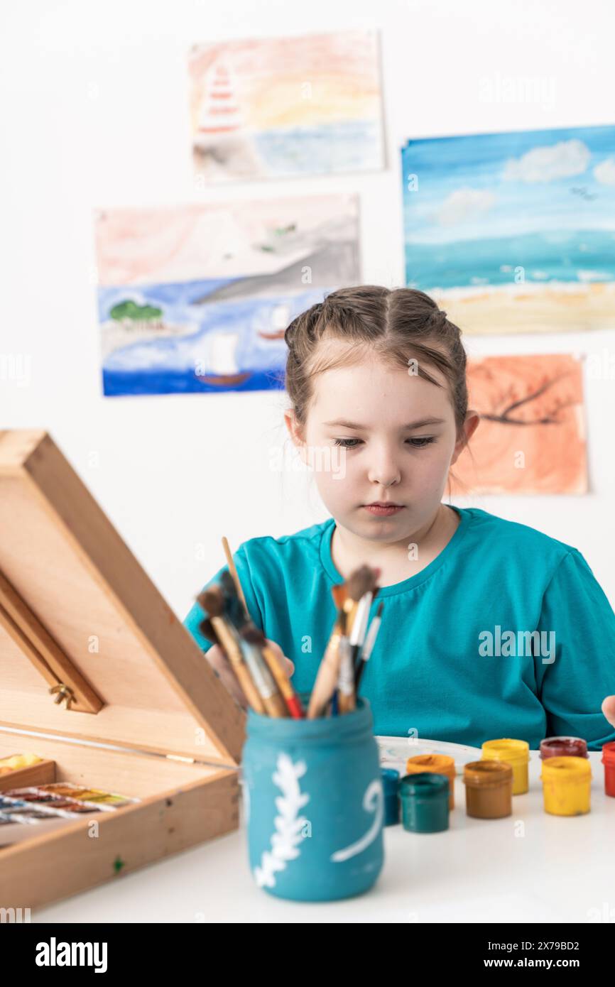 Little girl of pre-adolescence drawing on easel. Beautiful little girl ...