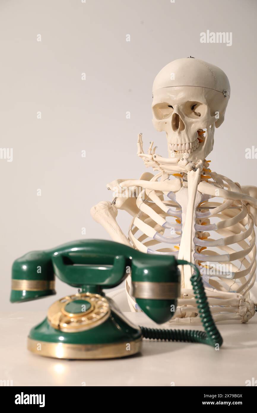 Waiting concept. Human skeleton at table with corded telephone against ...