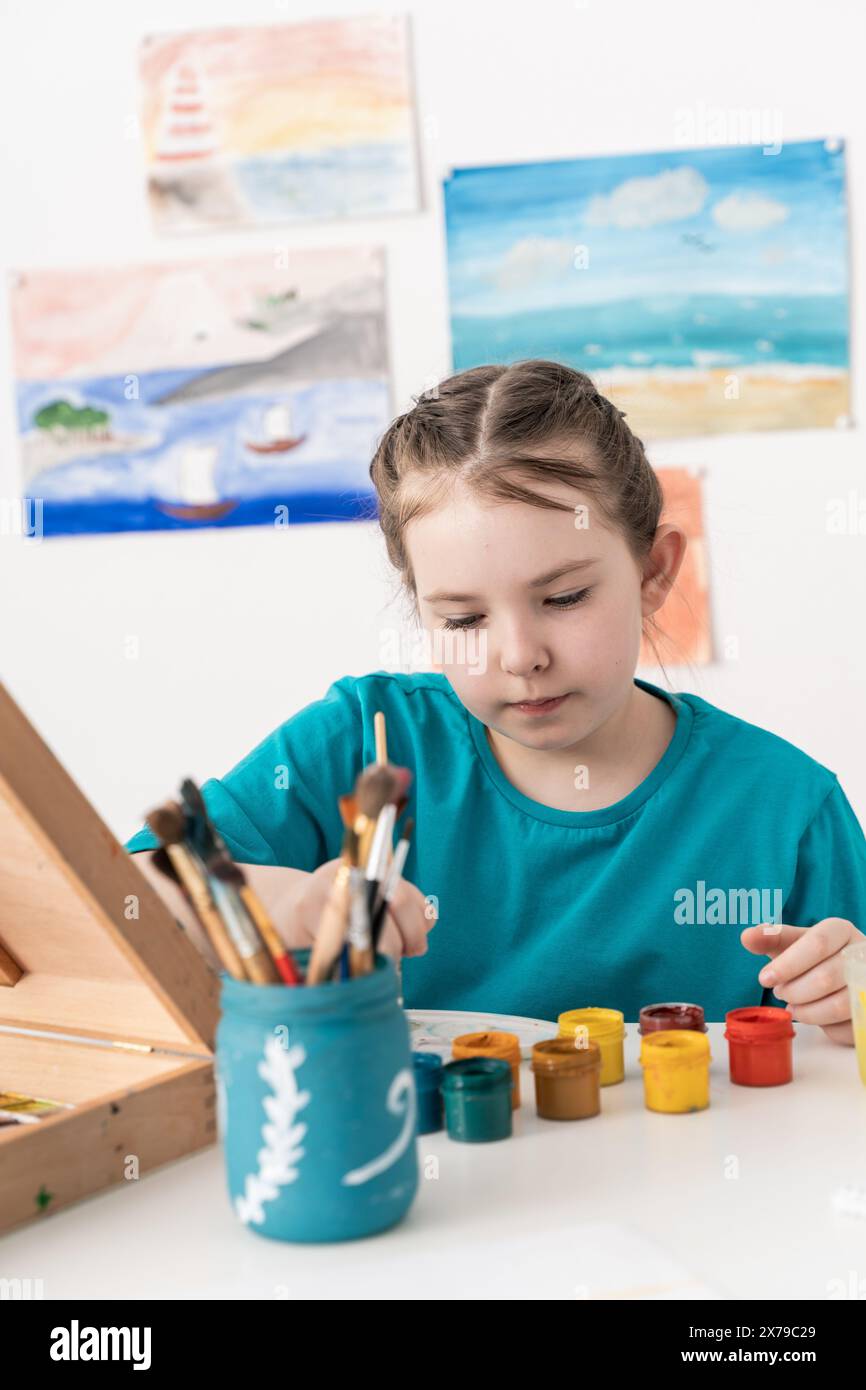 Little girl of pre-adolescence drawing on easel. Beautiful little girl ...