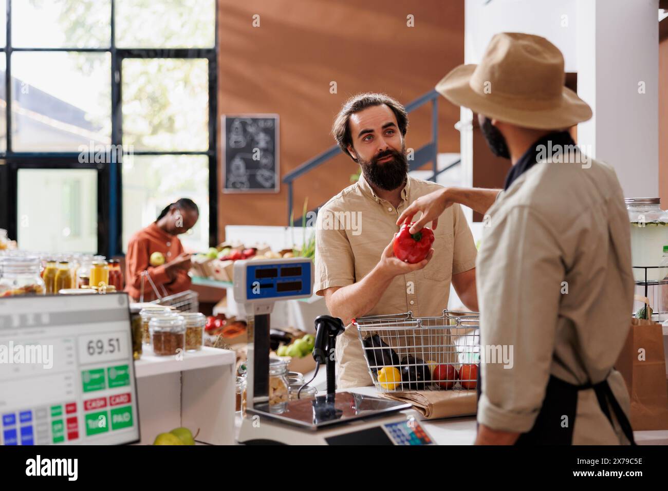 A young salesman wearing an apron and hat is helping caucasian customer ...