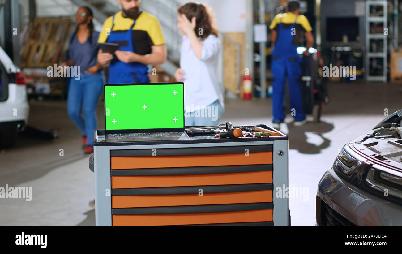 Green screen laptop placed on working bench in busy garage next to ...