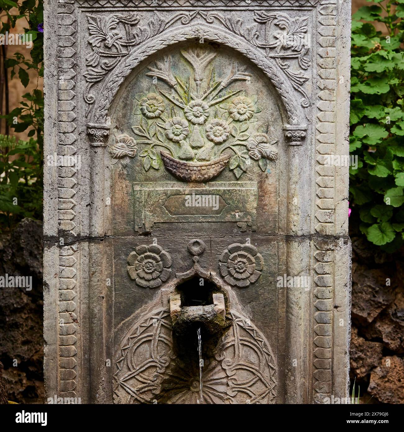 Artfully engraved stone fountain with plant motifs, water flowing out ...