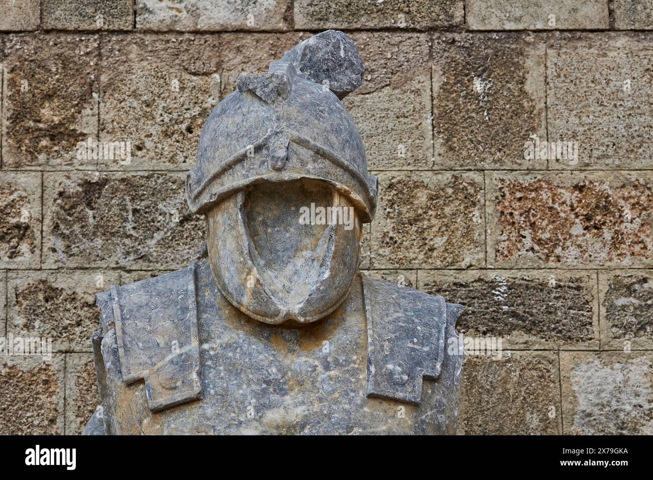 Stone figure of a headless knight in armour in front of a rustic wall ...