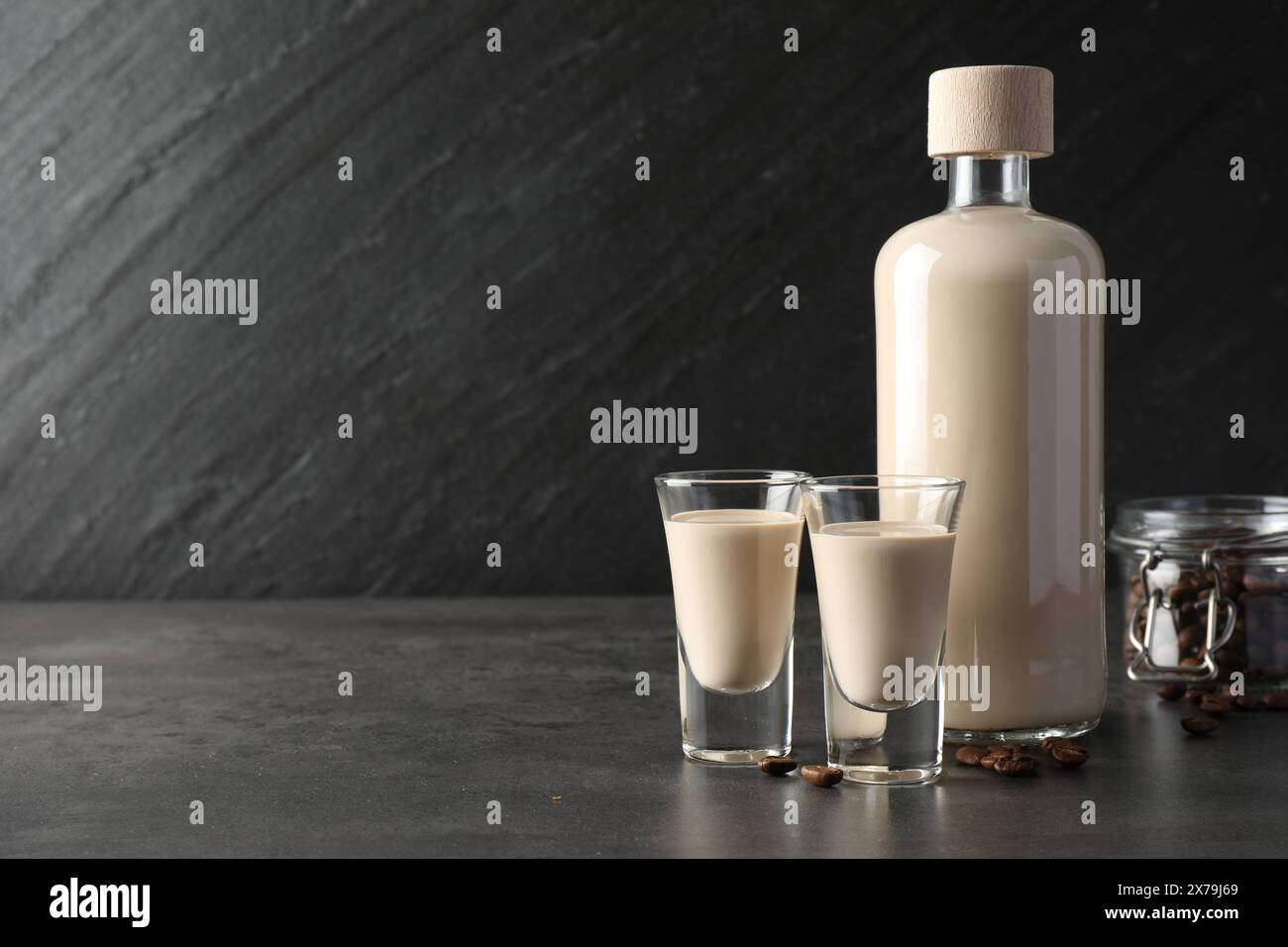 Coffee cream liqueur in glasses, bottle and beans on grey table, space ...