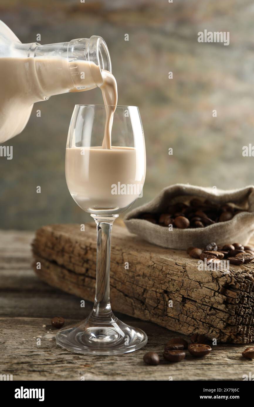 Pouring coffee cream liqueur into glass at wooden table, closeup Stock ...