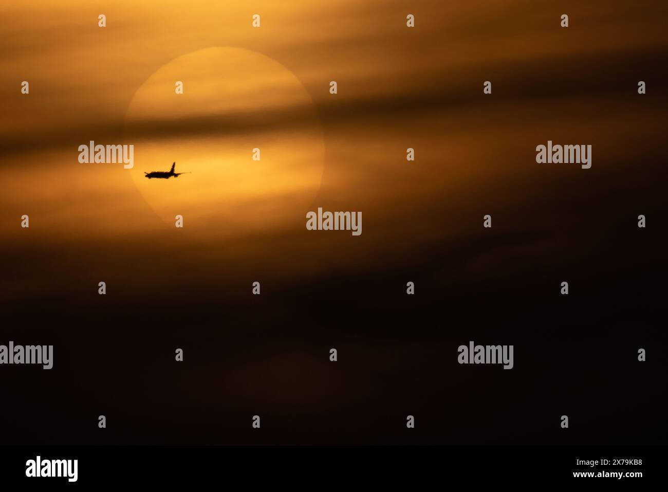 A passenger jet plane crosses the sun during a warm evening over London ...