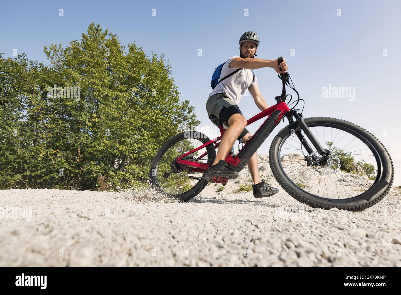 Male electric mountain bike rider going downhill and braking on a hilly rocky trail, low-angle ...