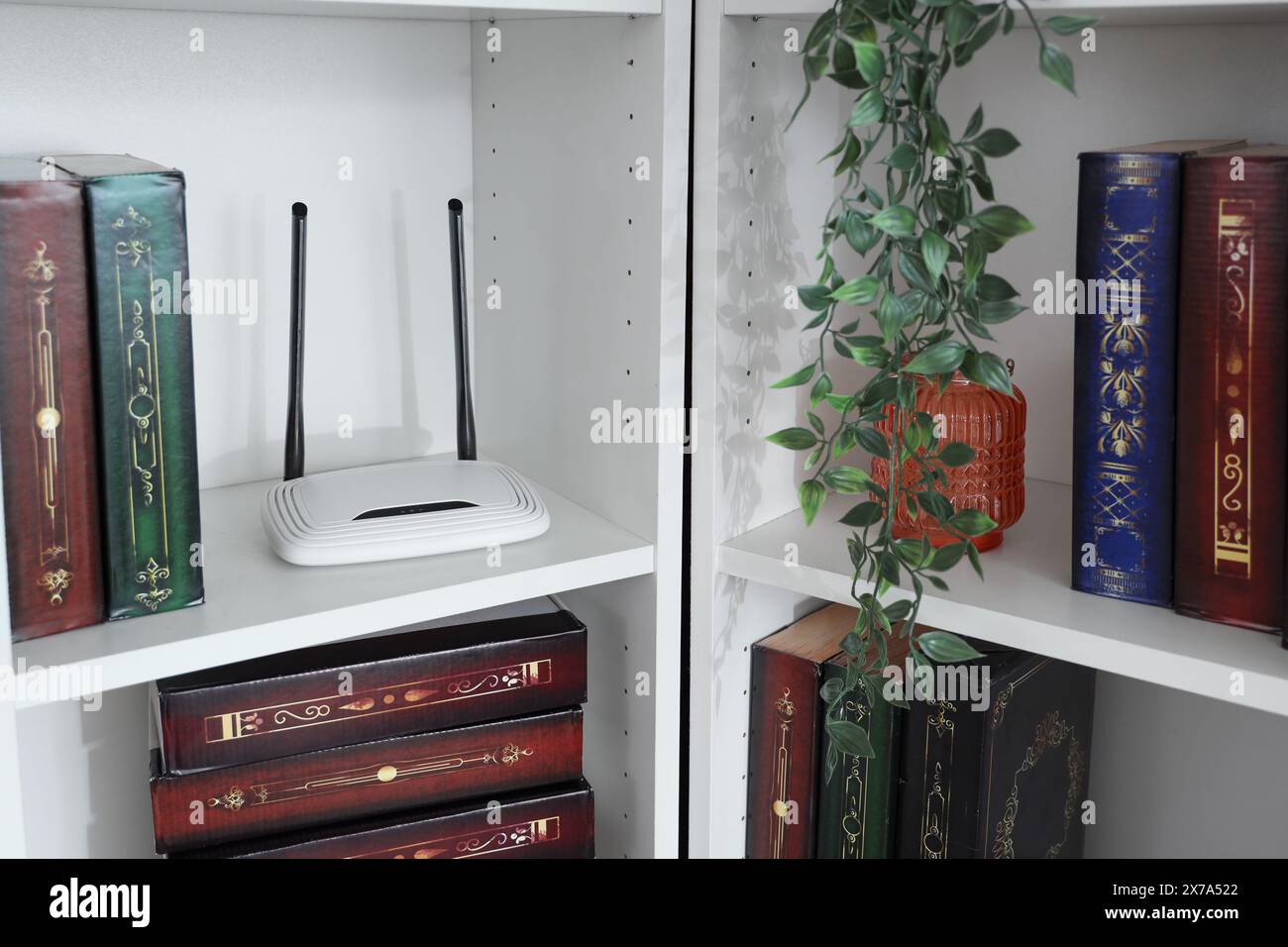 Bookshelf with modern wi-fi router in room, closeup Stock Photo - Alamy