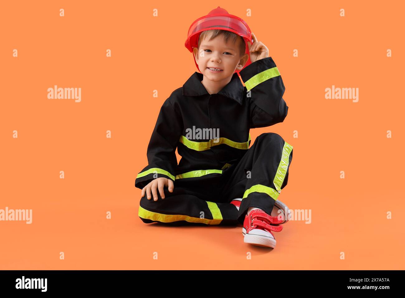 Cute little firefighter sitting on orange background Stock Photo - Alamy