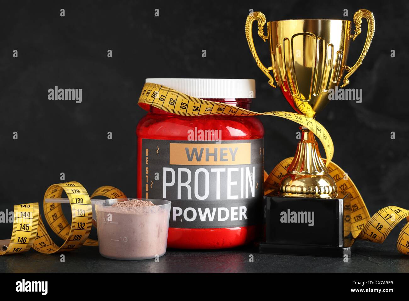 Bottle of protein powder, gold cup and measuring tape on dark ...