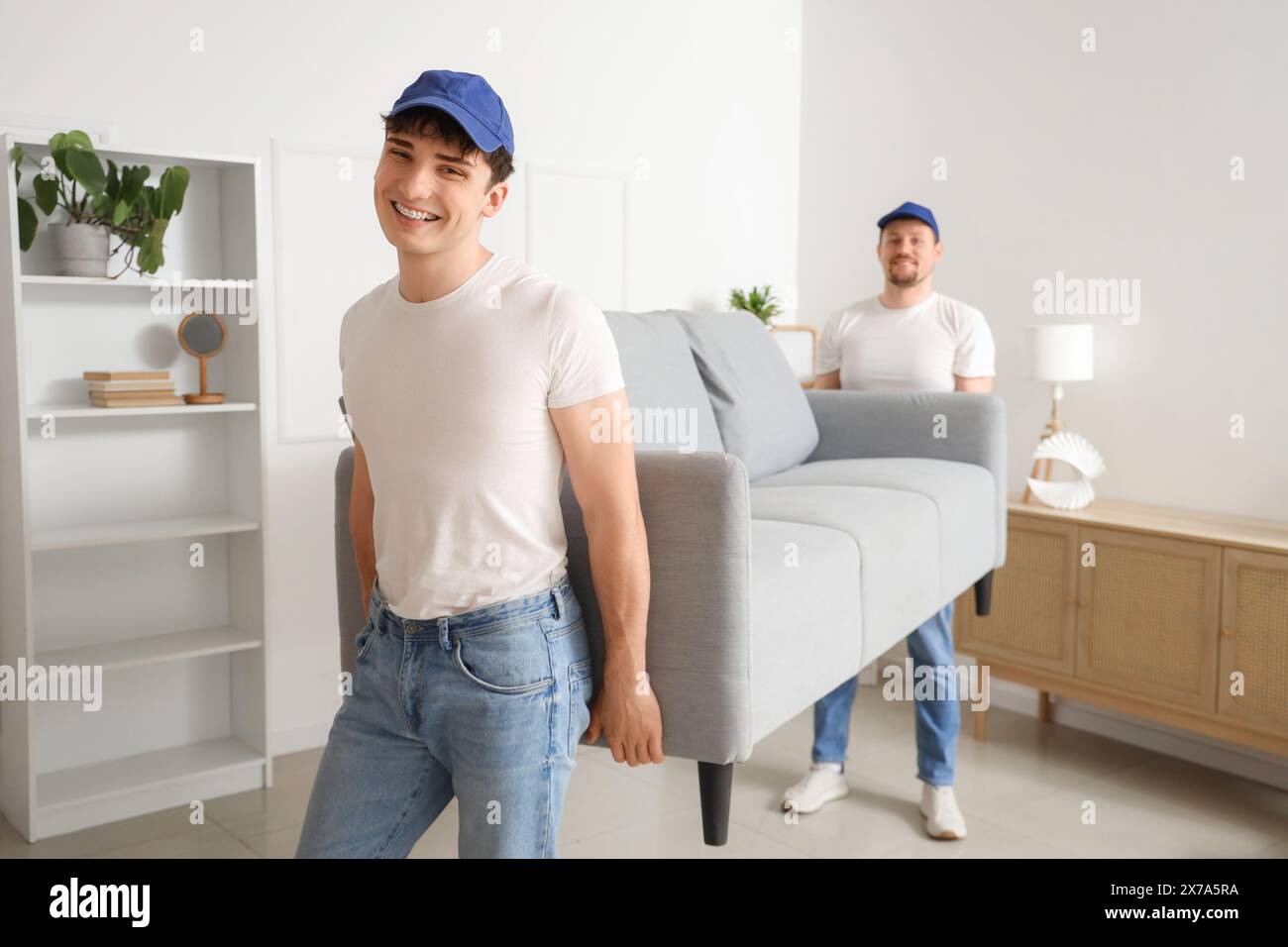 Loaders carrying sofa in room Stock Photo - Alamy