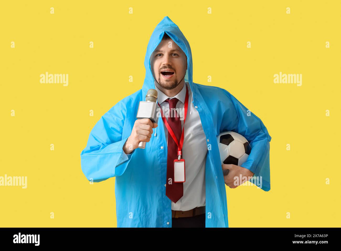 Male reporter in raincoat with microphone and soccer ball on yellow ...