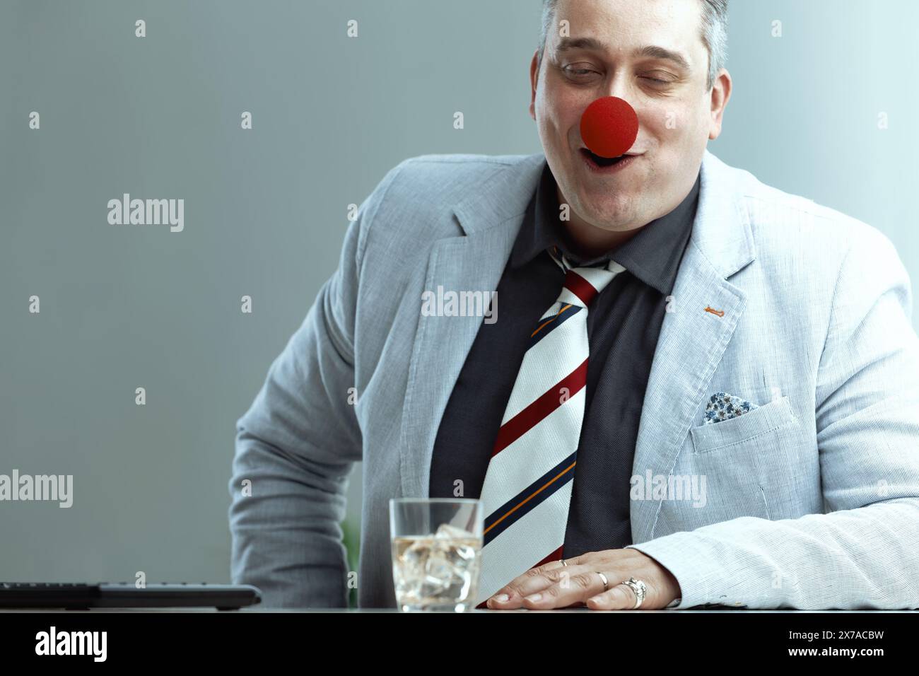 middle-aged man with a clown nose and spiky gray hair leans over a ...