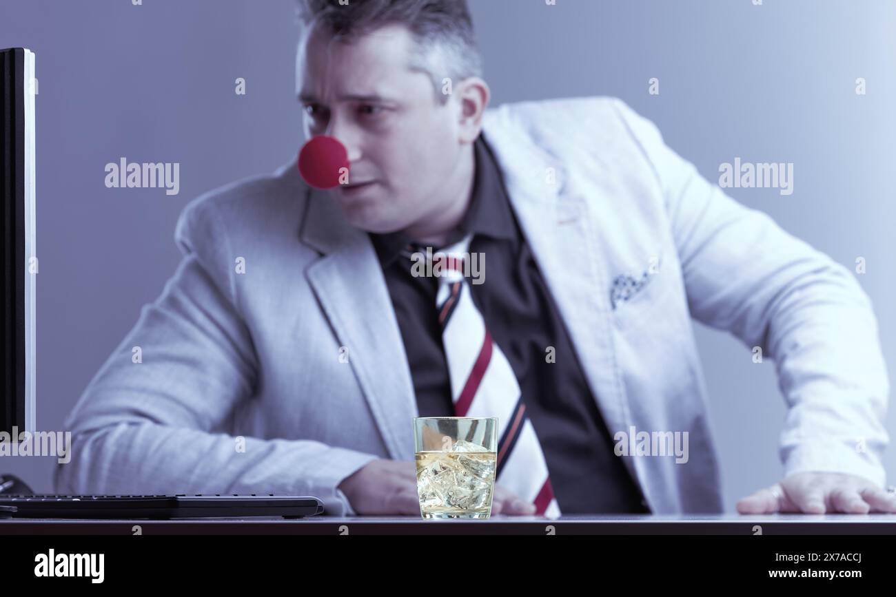 Man with spiky gray hair wearing a clown nose leans over a desk ...