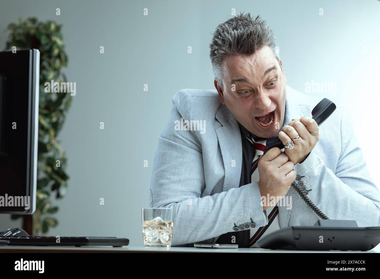middle-aged man in a light suit and striped tie yells angrily into a ...