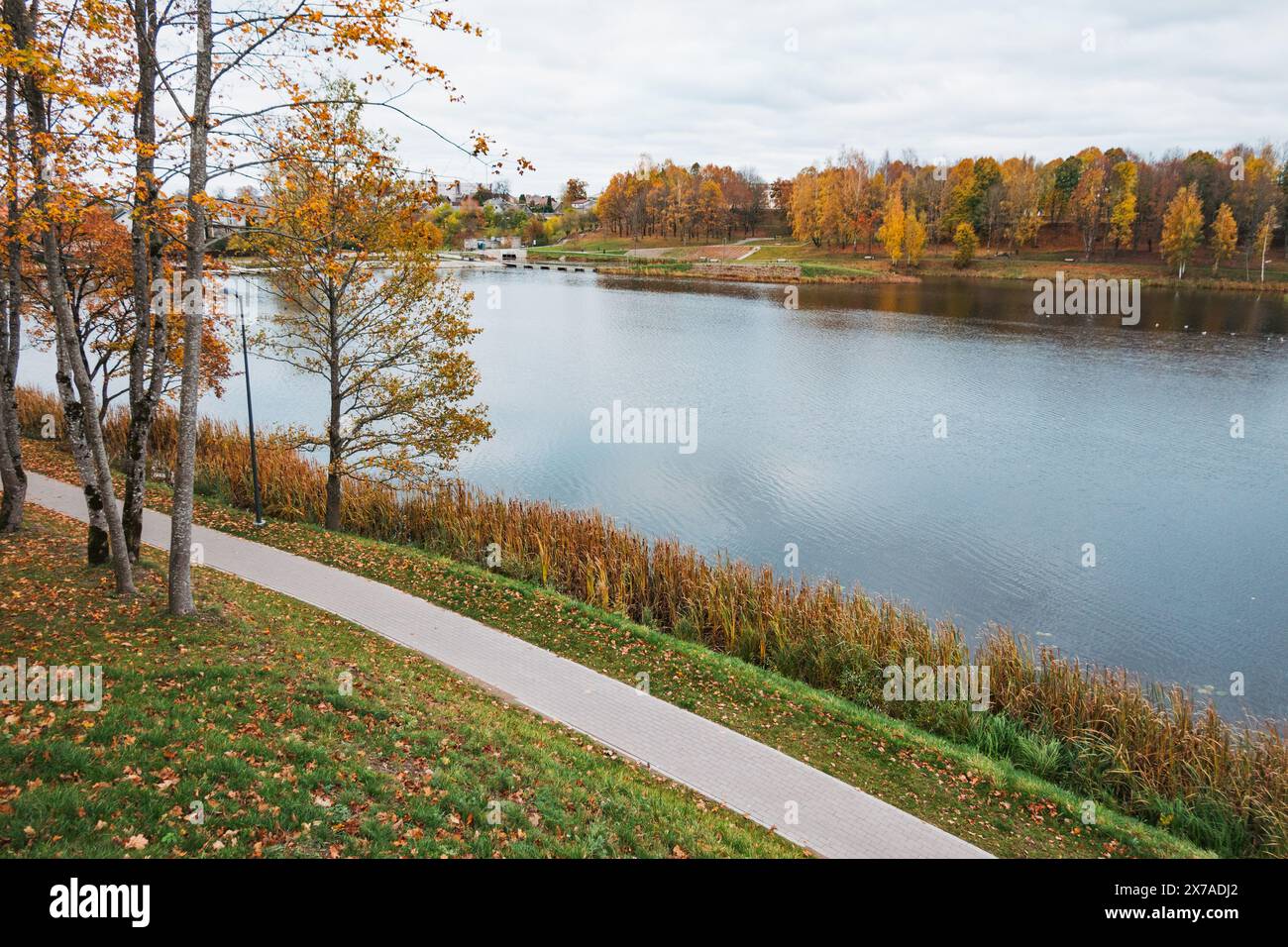 a walking path goes around the edge of a lake on a calm but cloudy ...