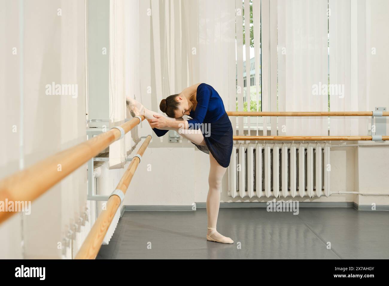 Dancer stretching leg muscles, bending her body forward and pressing ...