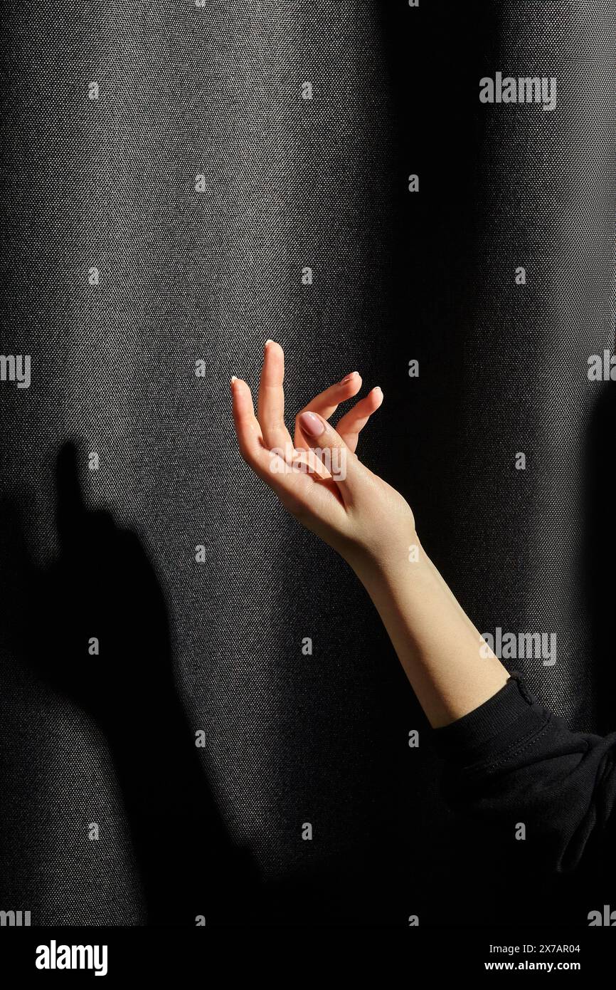 Elegant female hand poised against dark fabric with shadow Stock Photo ...