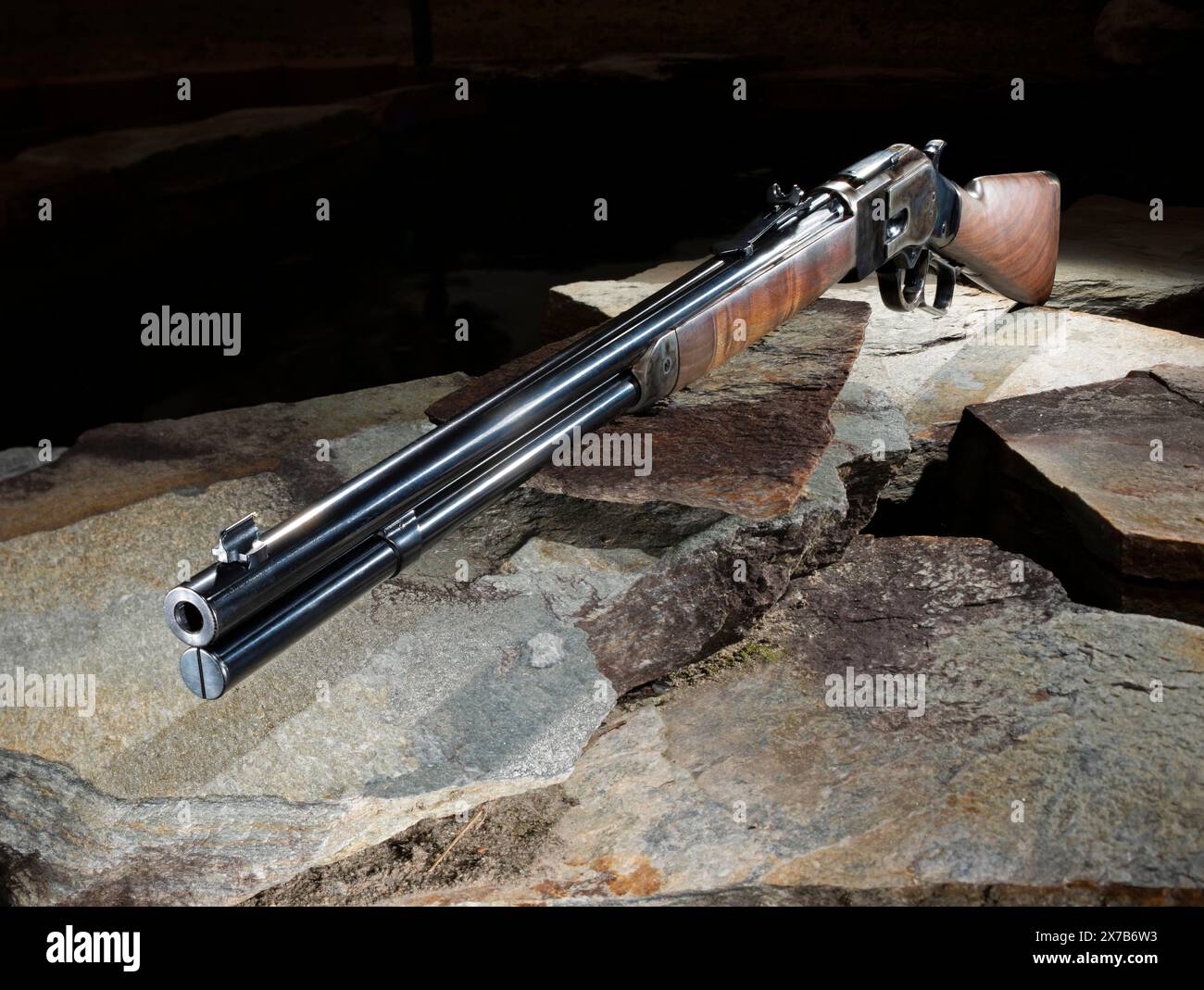 Lever action rifle with wood stocks sitting on stones with a dark ...